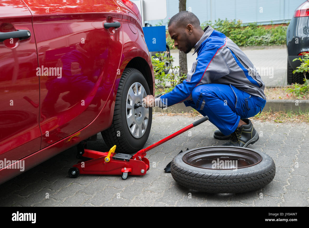 Jeune Mécanicien africain changer pneu d'une voiture rouge avec une clé Photo Stock - Alamy