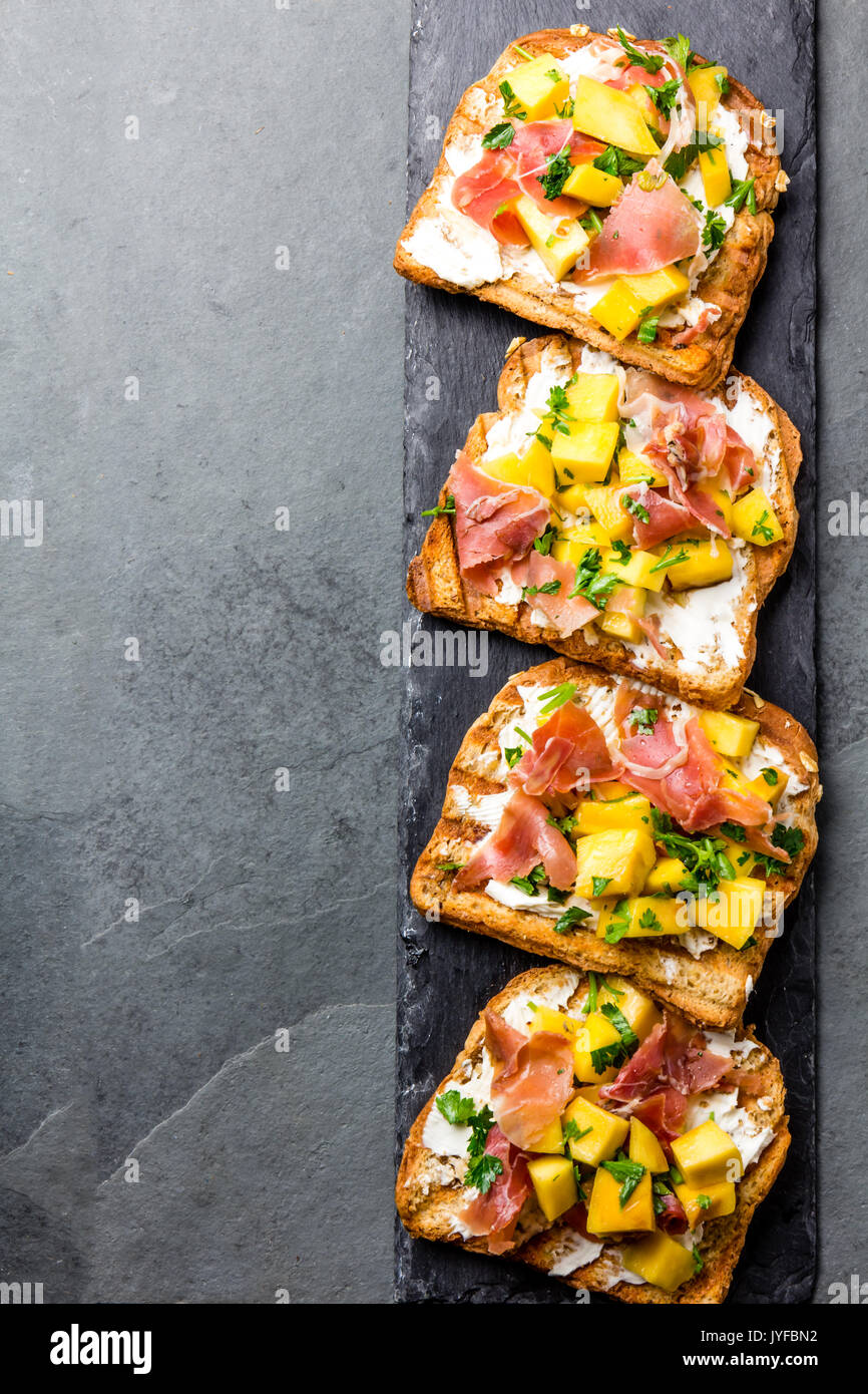 Toasts avec du fromage à la crème, jambon jamon serrano et mangue servi ...