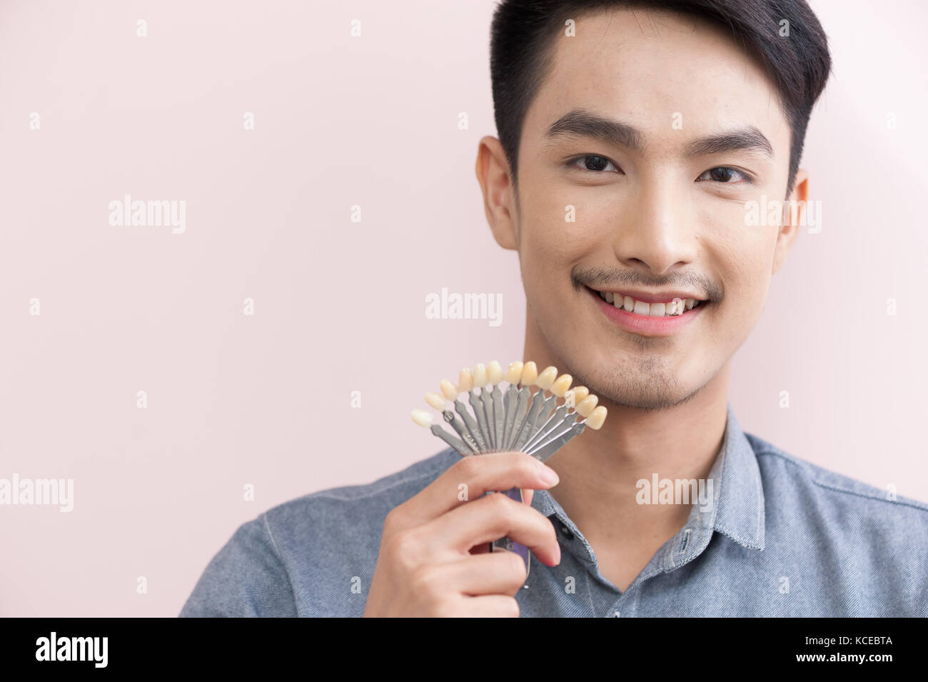 Asian male smiling while holding exemples couleur dent dans sa main ...