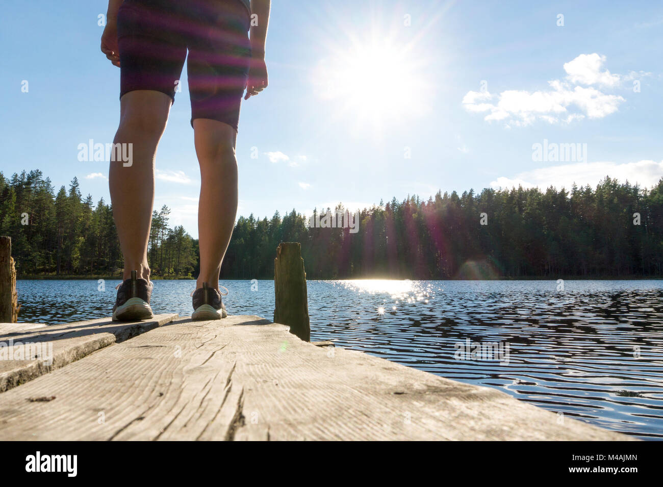 Jeune femme debout sur un vieux quai en bois et d'une jetée à un lac à l'été en Finlande. Soleil ...