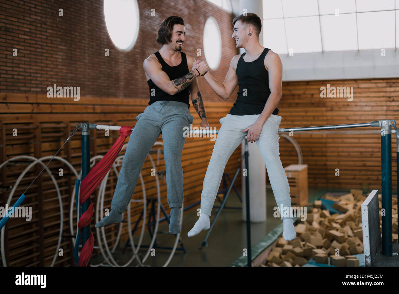 Deux gymnastes souriant assis sur high bar shaking hands in gym Photo ...