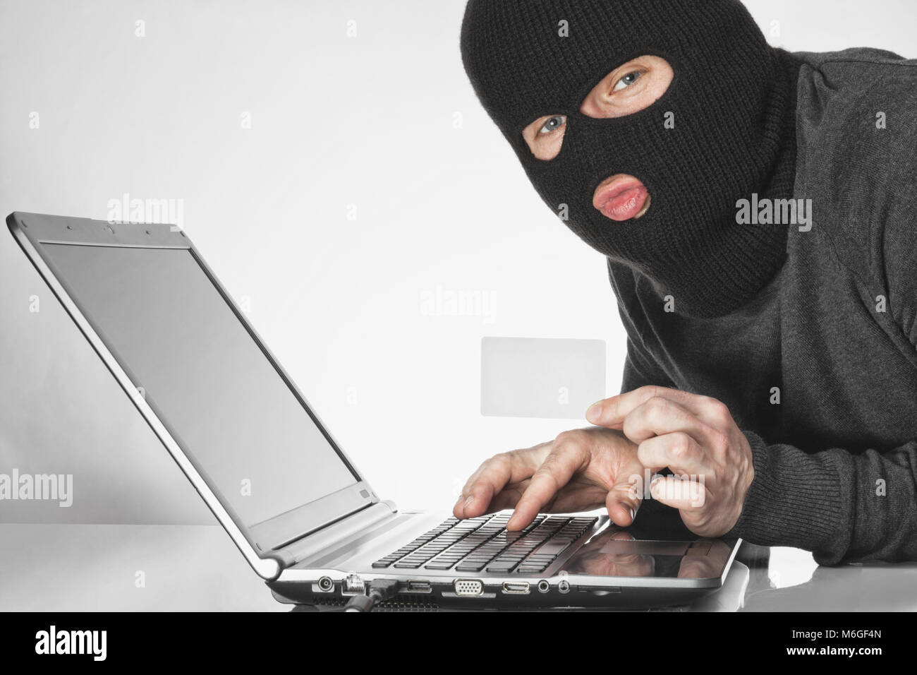 Hacker mâle à balaclava tenant une carte dans la main gauche et tapant ...