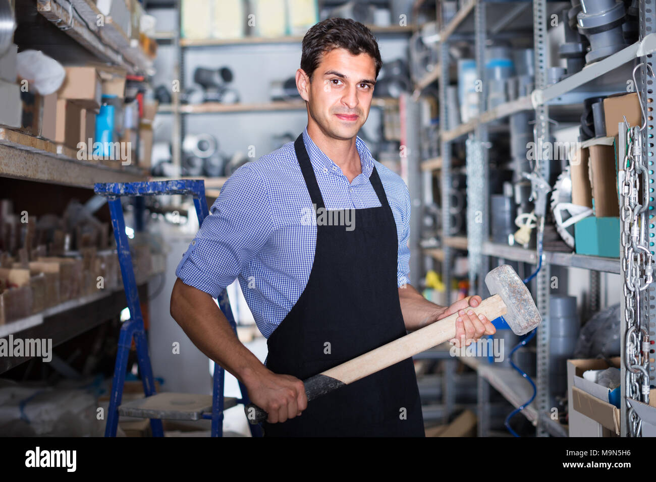 Portrait d'homme en uniforme qui est debout avec sledgehammer dans la construction d'atelier ...