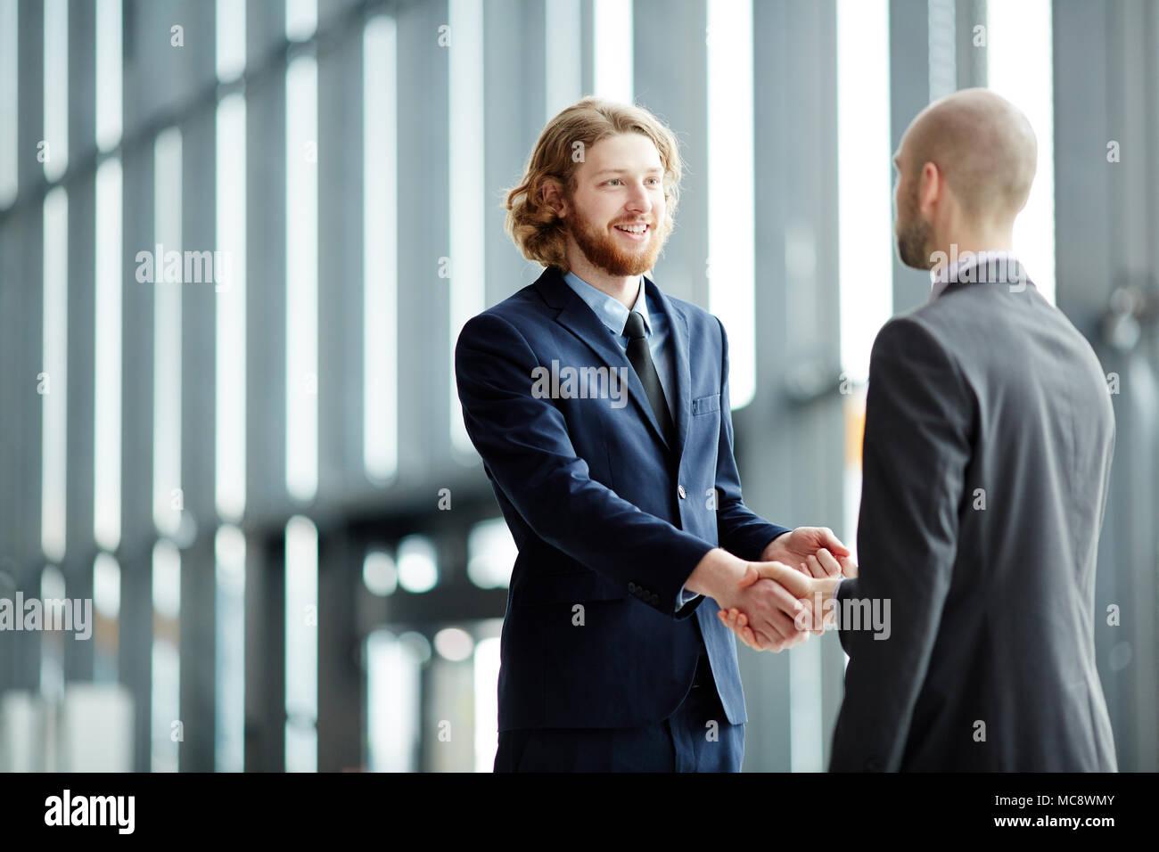 Deux jeunes hommes en costumes se saluer par handshake après ...