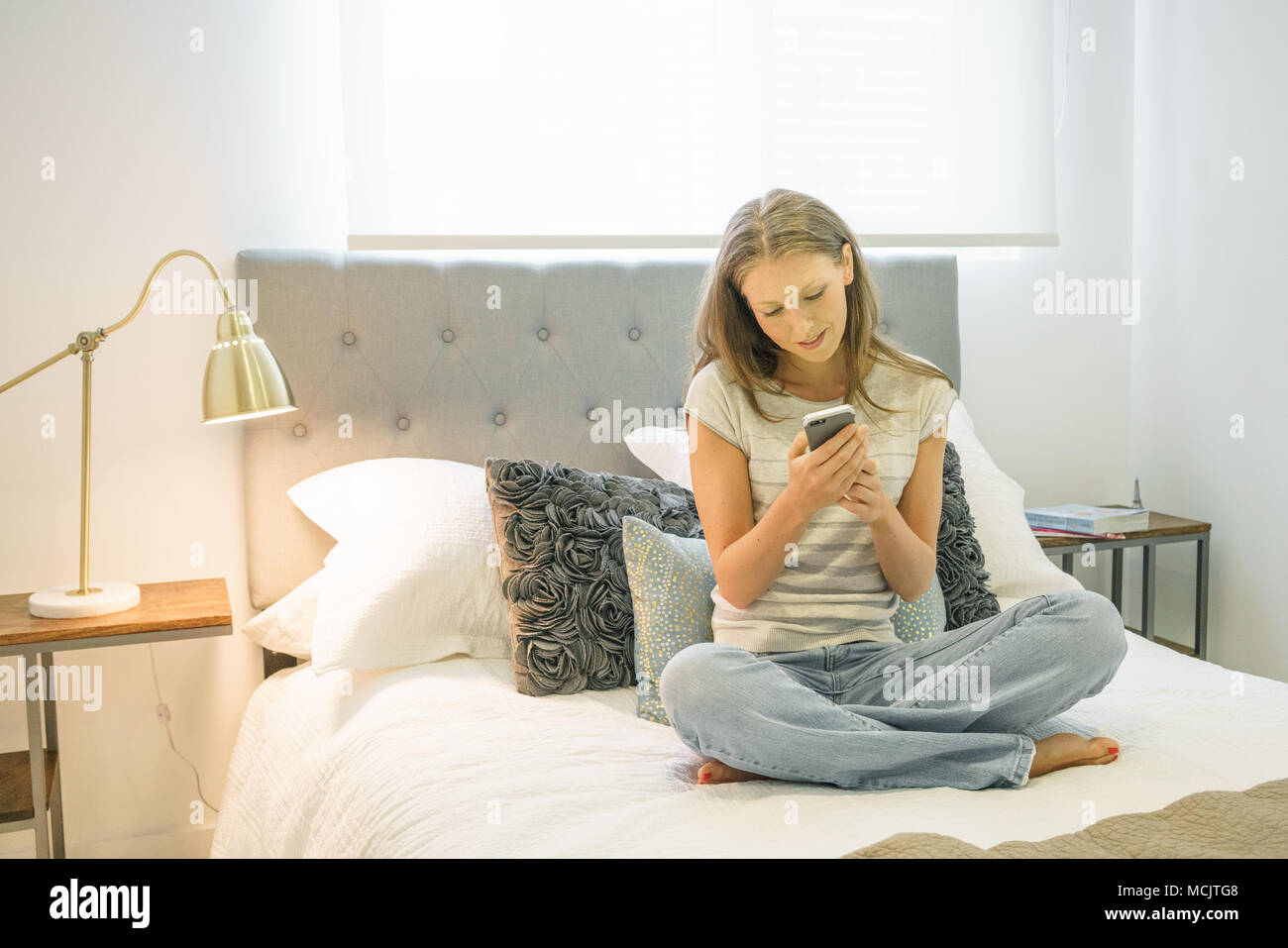 Jeune Femme Assise En Tailleur Sur Le Lit Banque De Photographies Et D