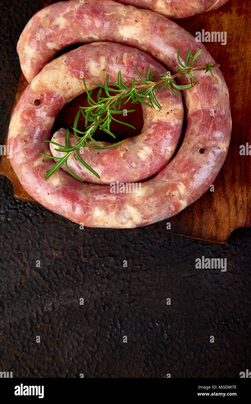Spirale de matières premières saucisses de porc au romarin, sel et poivre sur planche à découper ...