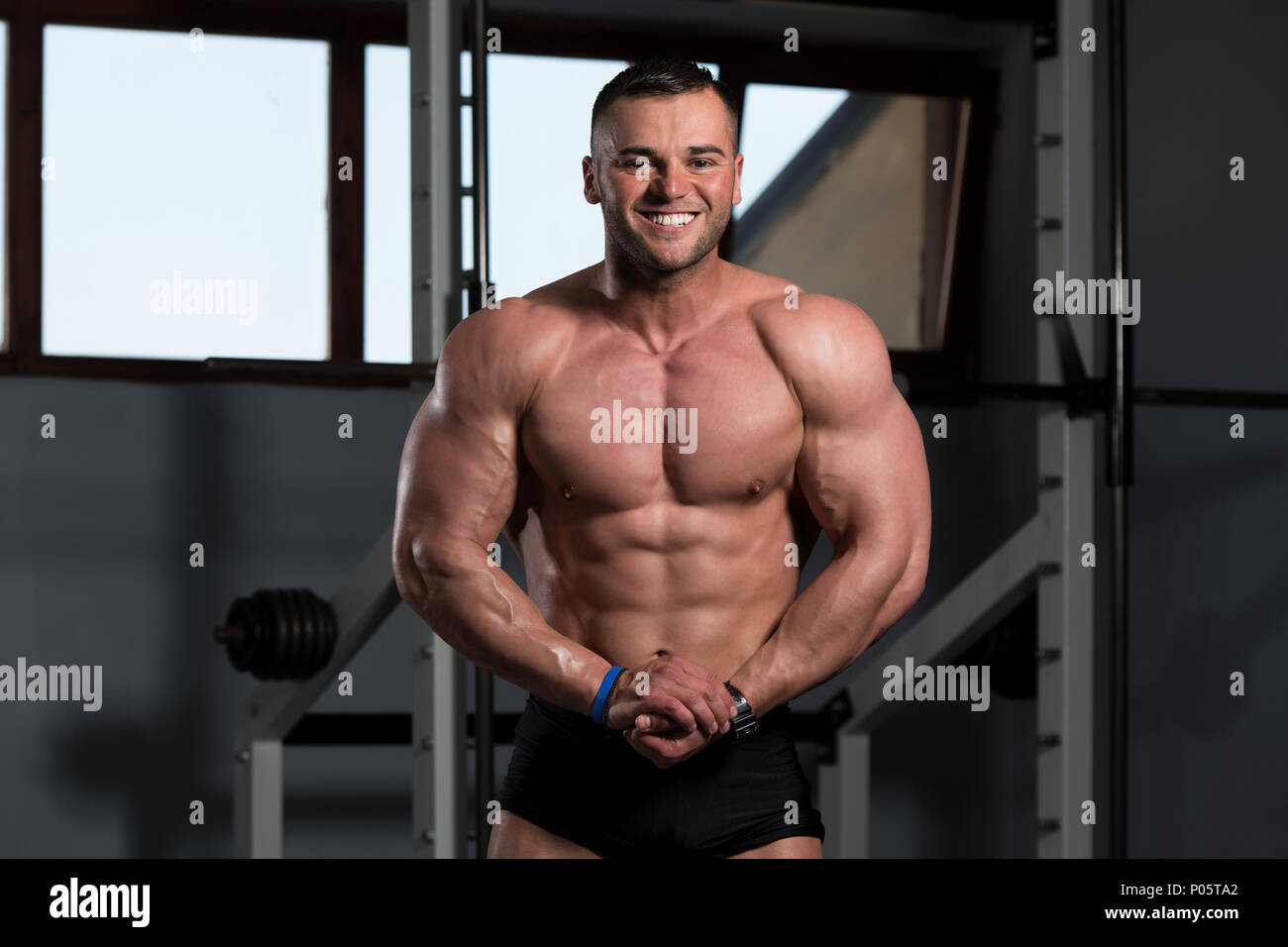 Jeune homme debout forte dans la salle de sport et Flexing Muscles ...