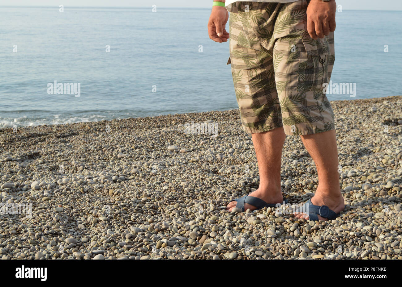 Les jambes de l'homme en tongs et shorts, un homme debout sur la plage ...