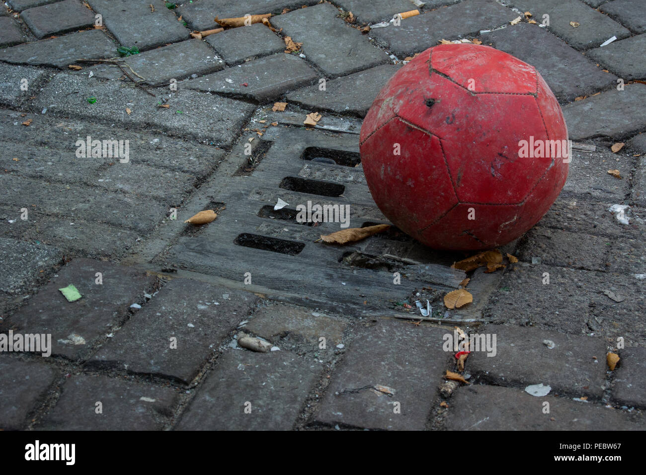 Un ballon de soccer rouge usé s'installe dans la grille d'une gouttière ...