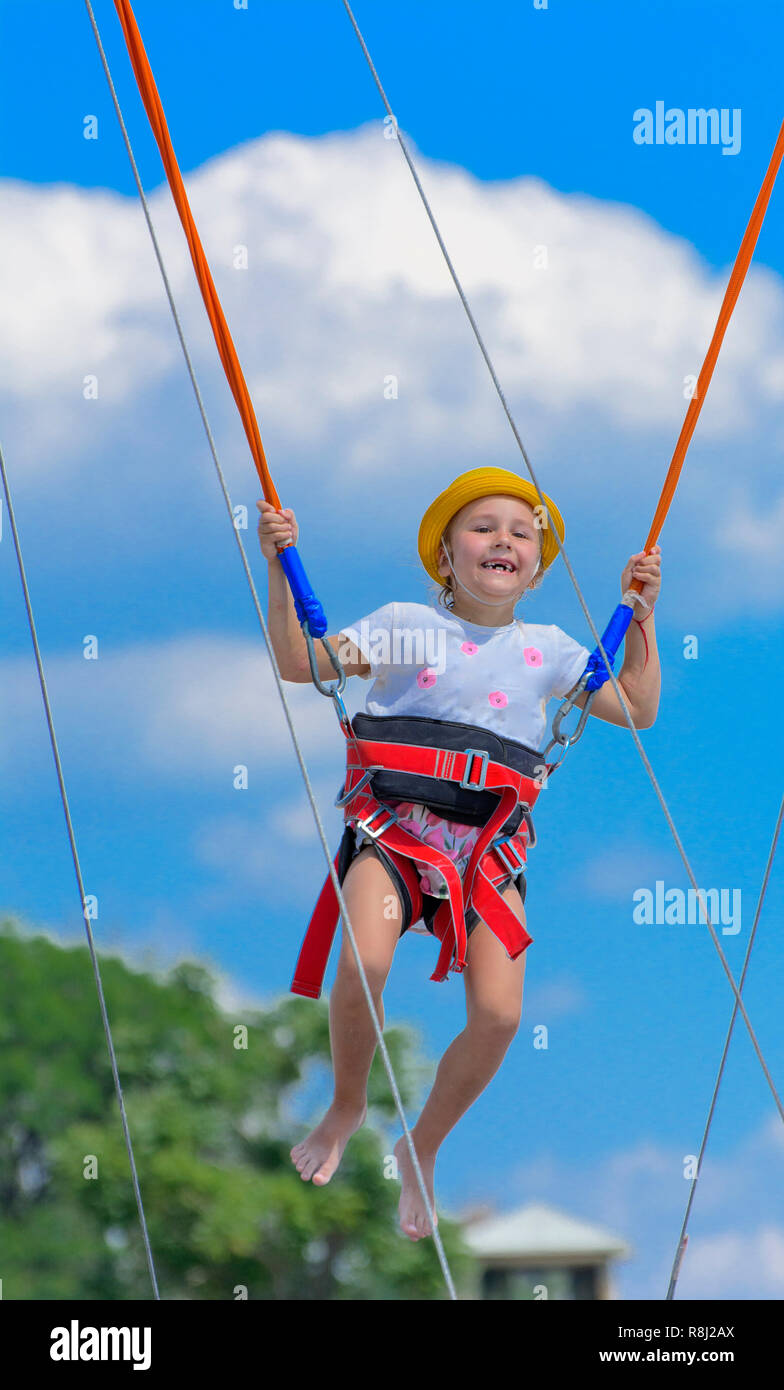 Une petite fille saute sur un trampoline haut avec des cordes en ...