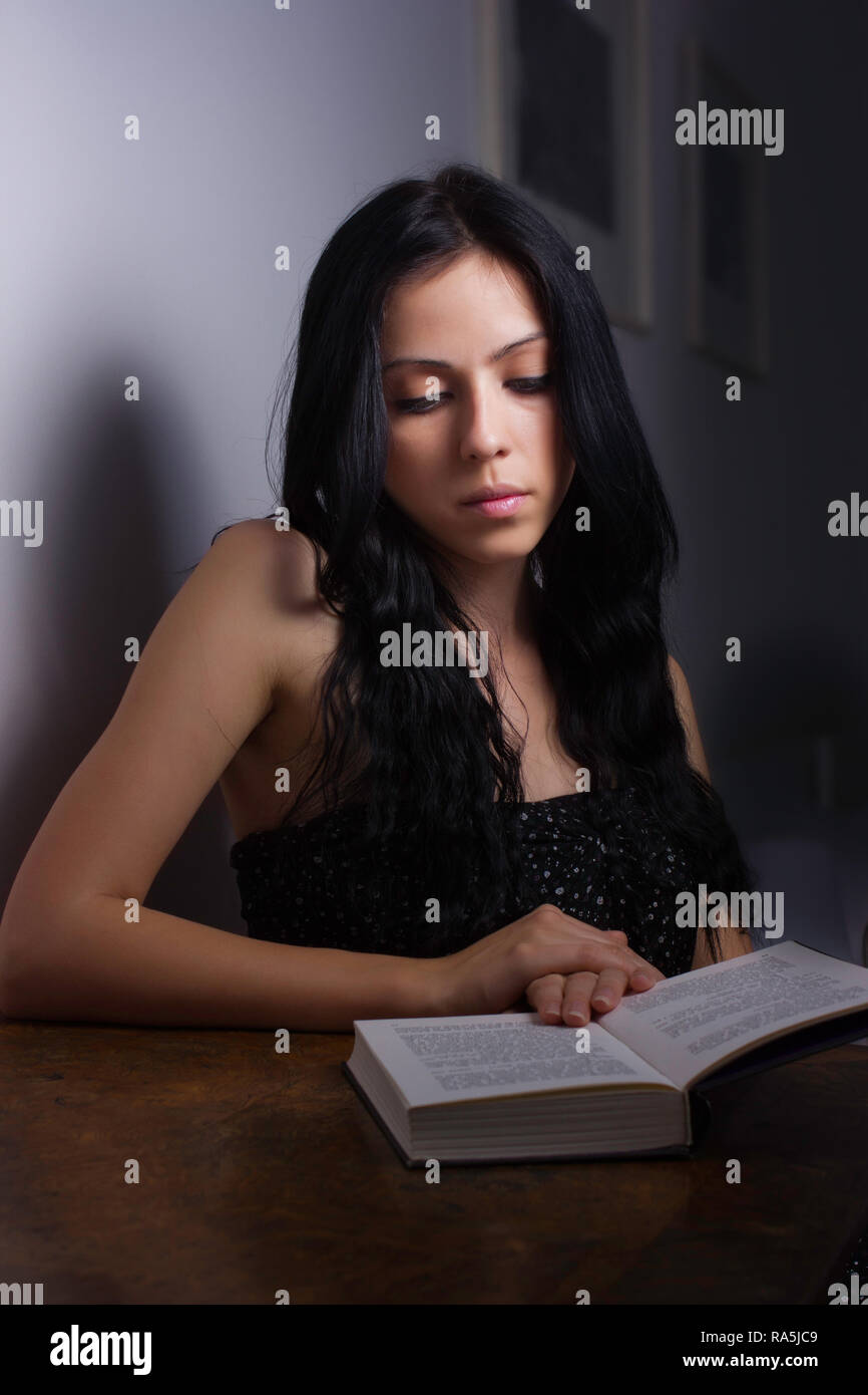 Jeune fille assise dans la chaise à côté de bureau et la lecture de livre, fleurs nad mirror en ...
