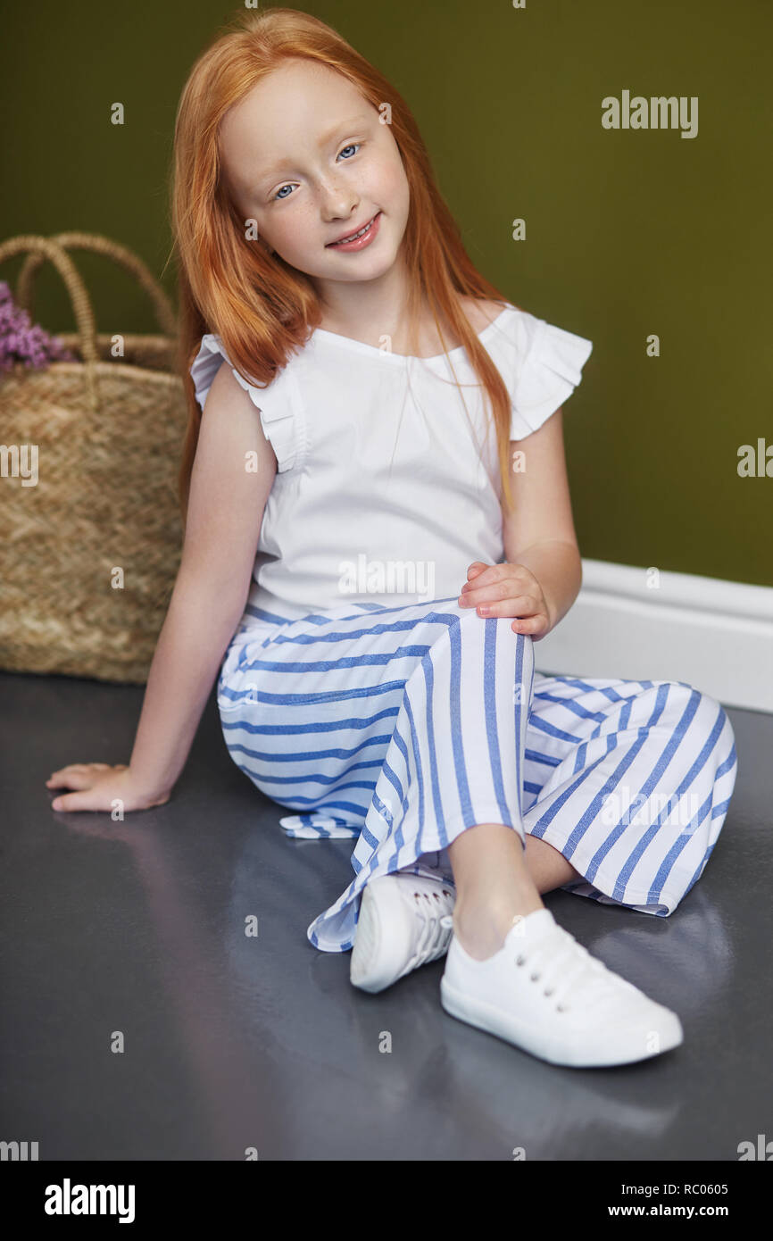 Petite fille rousse avec un panier de fleurs posant sur un fond d'olive ...