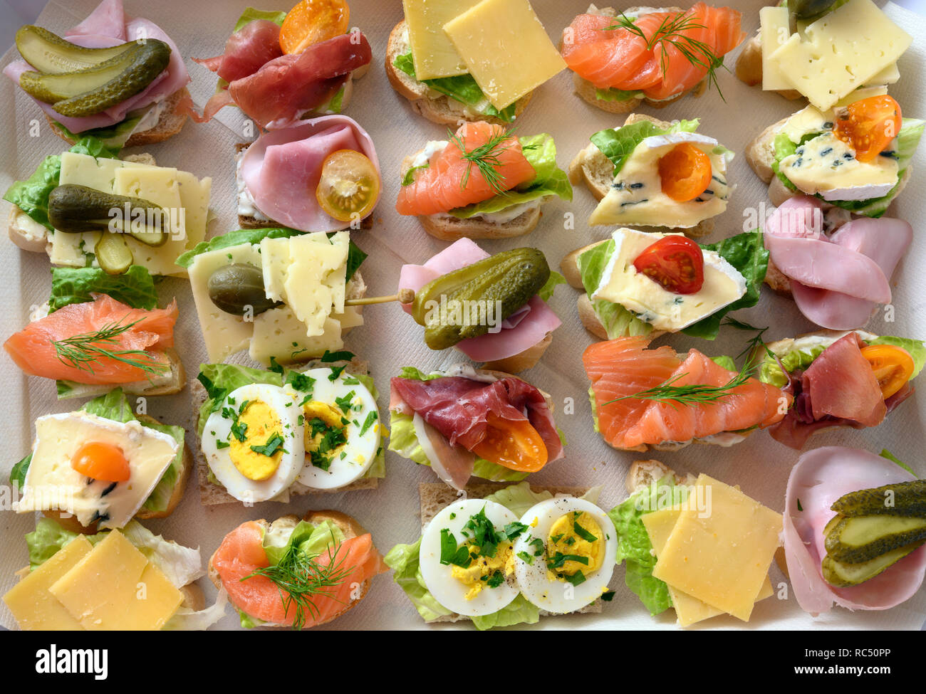 Canapés divers avec des œufs, du fromage, du jambon et du saumon sur un ...