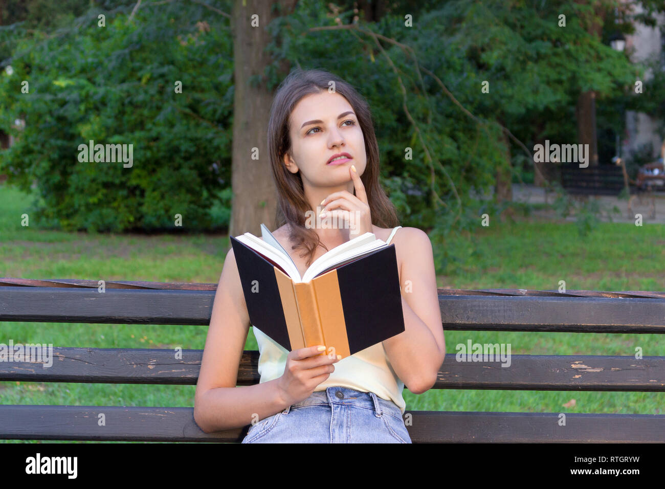 Belle femme est en train de lire un livre et de penser à quelque chose sur le banc dans le parc ...