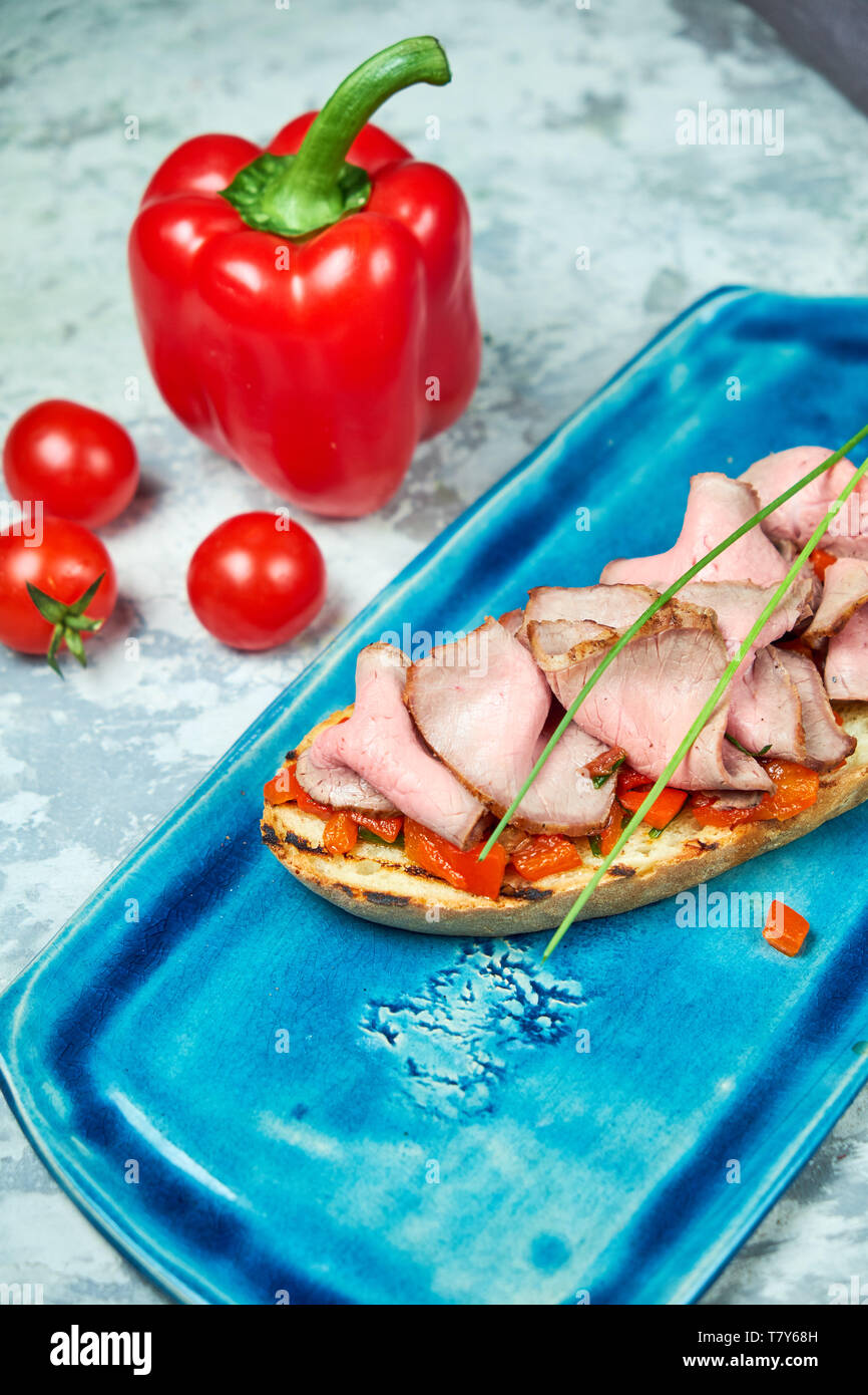Sur une plaque bleue de bruschet avec le boeuf et les tomates, à côté c ...