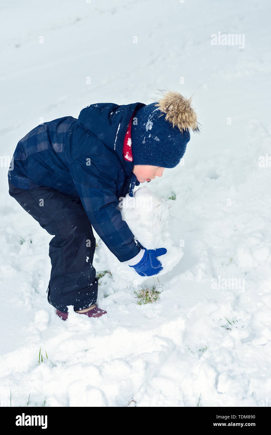 Petit garçon fait un bonhomme de neige en hiver. L'enfant roule une ...