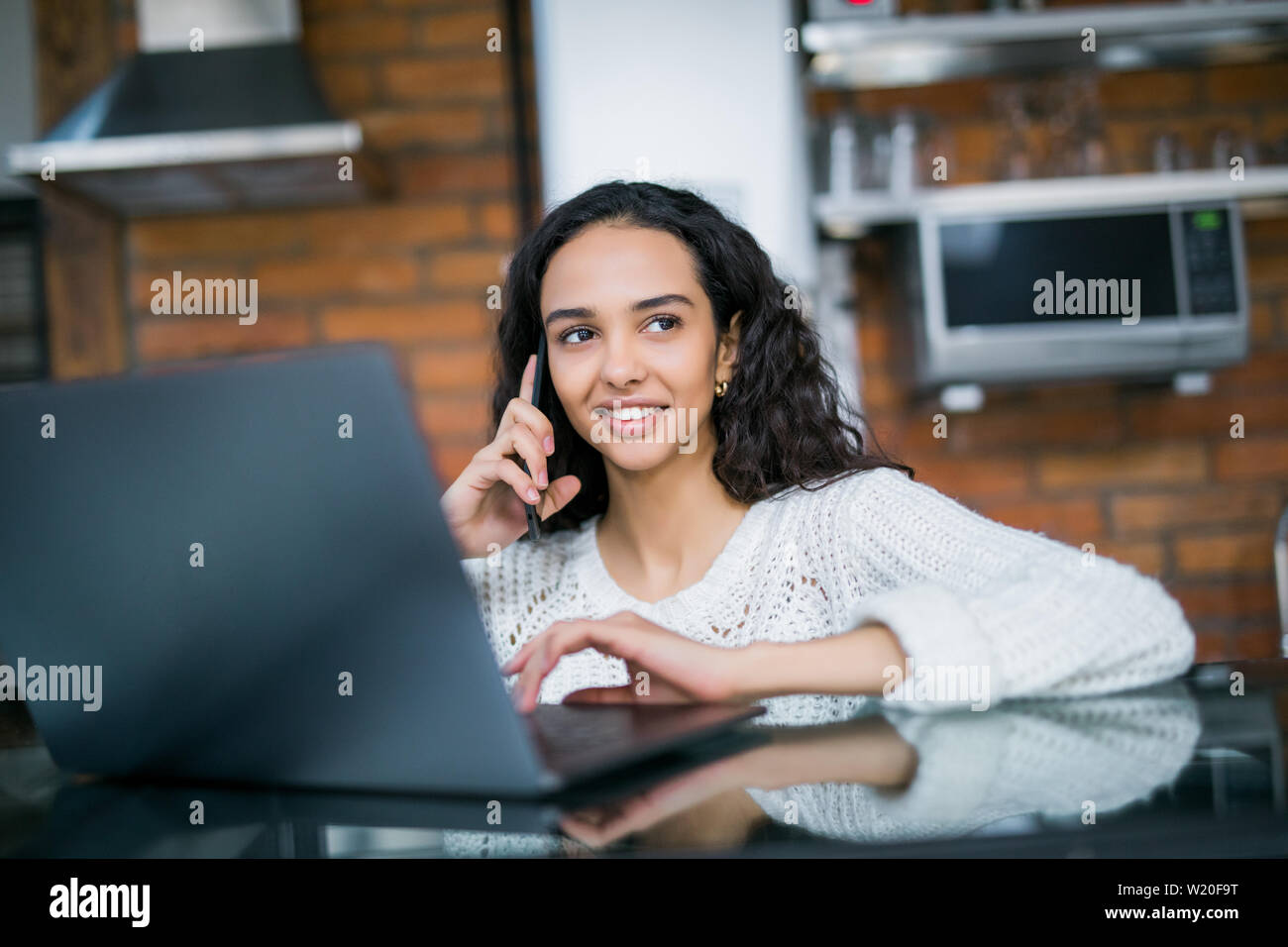 Jeune femme assise à la table de cuisine à l'aide d'un ordinateur ...
