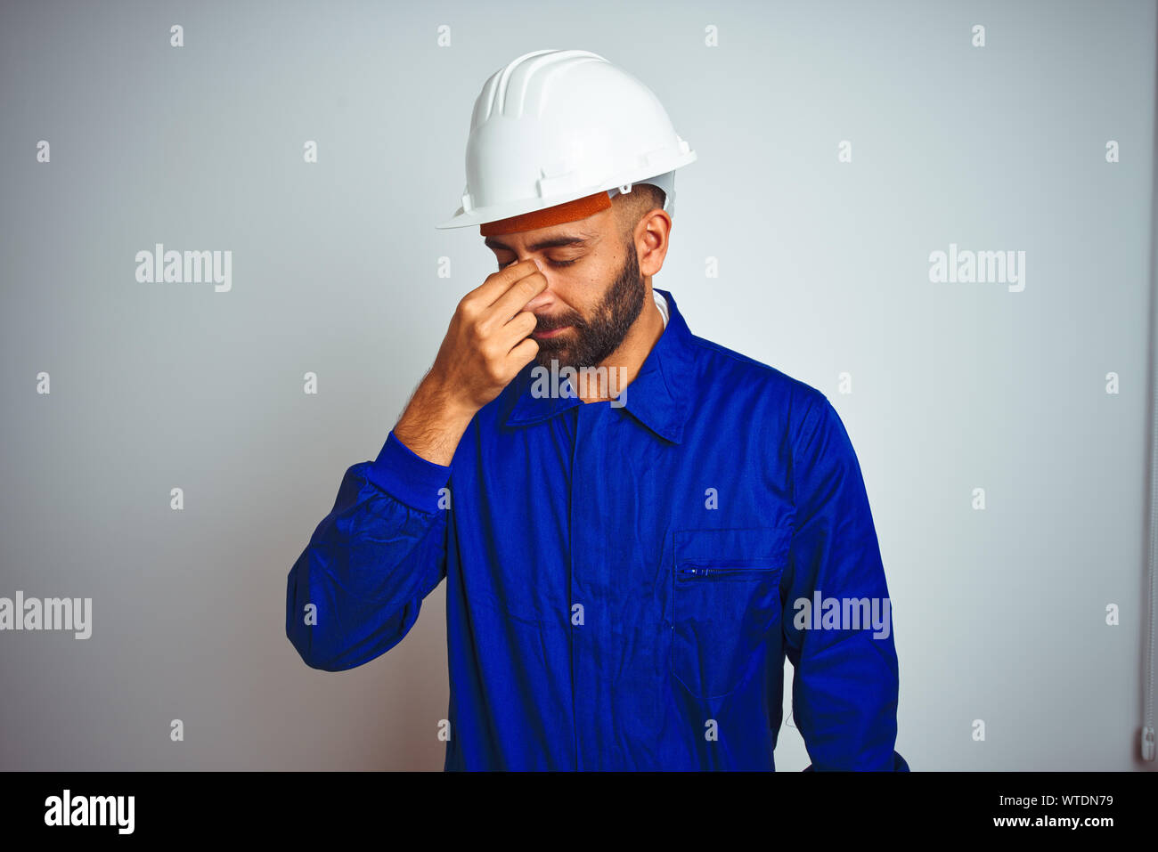Beau travailleur indien homme portant uniforme et casque sur fond blanc isolé fatigué se ...