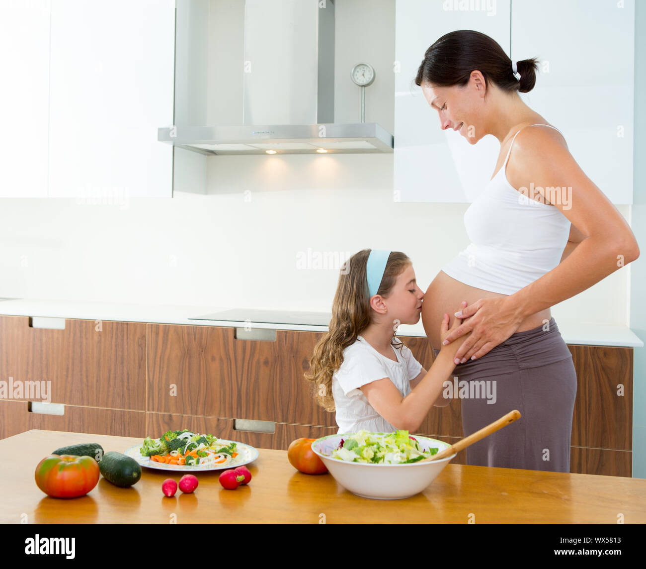 Belle mère enceinte avec sa fille au ventre en embrassant bébé cuisine Photo Stock - Alamy