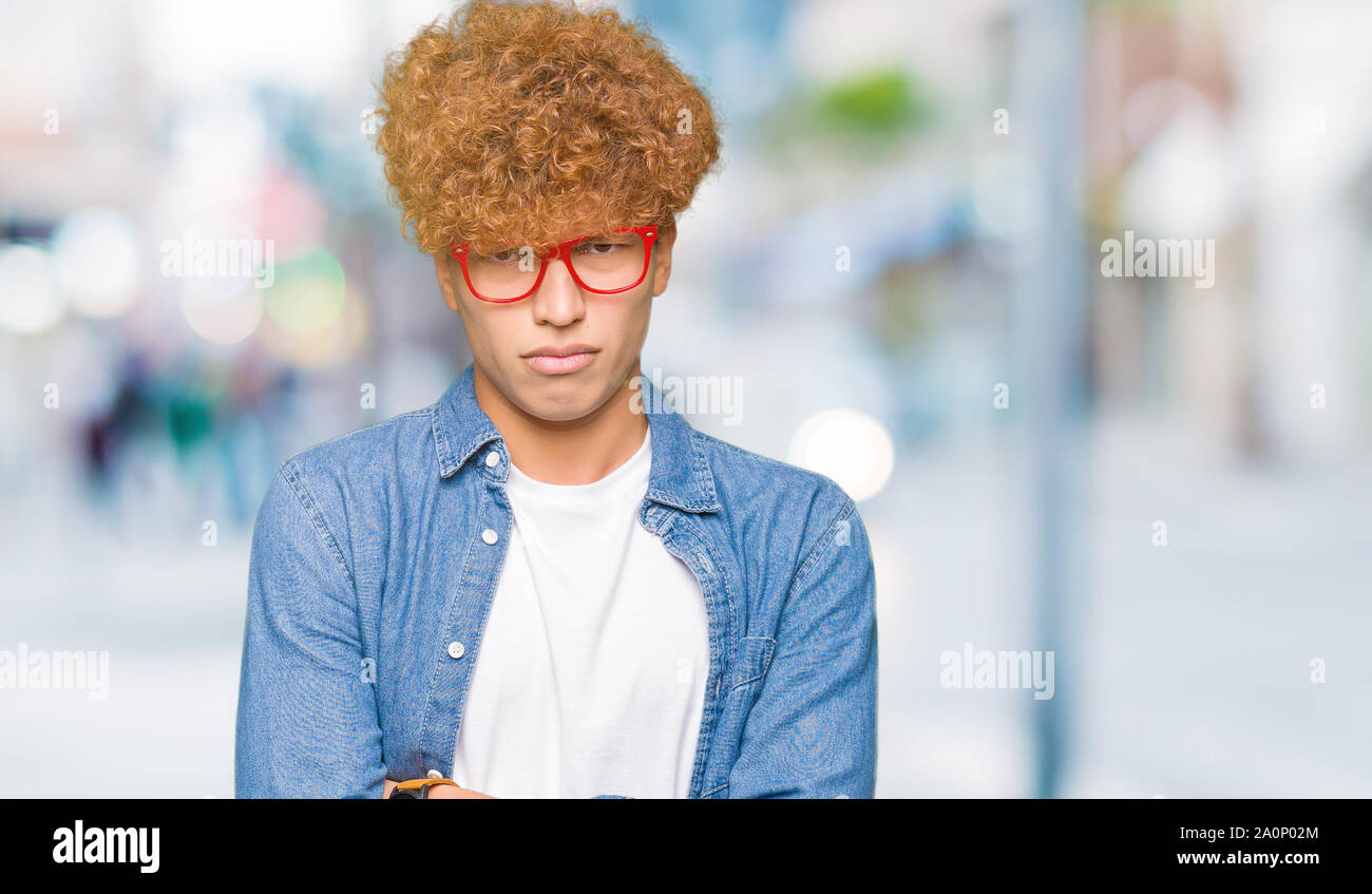 Giovane uomo bello con capelli Afro indossa occhiali scettico e nervoso ...