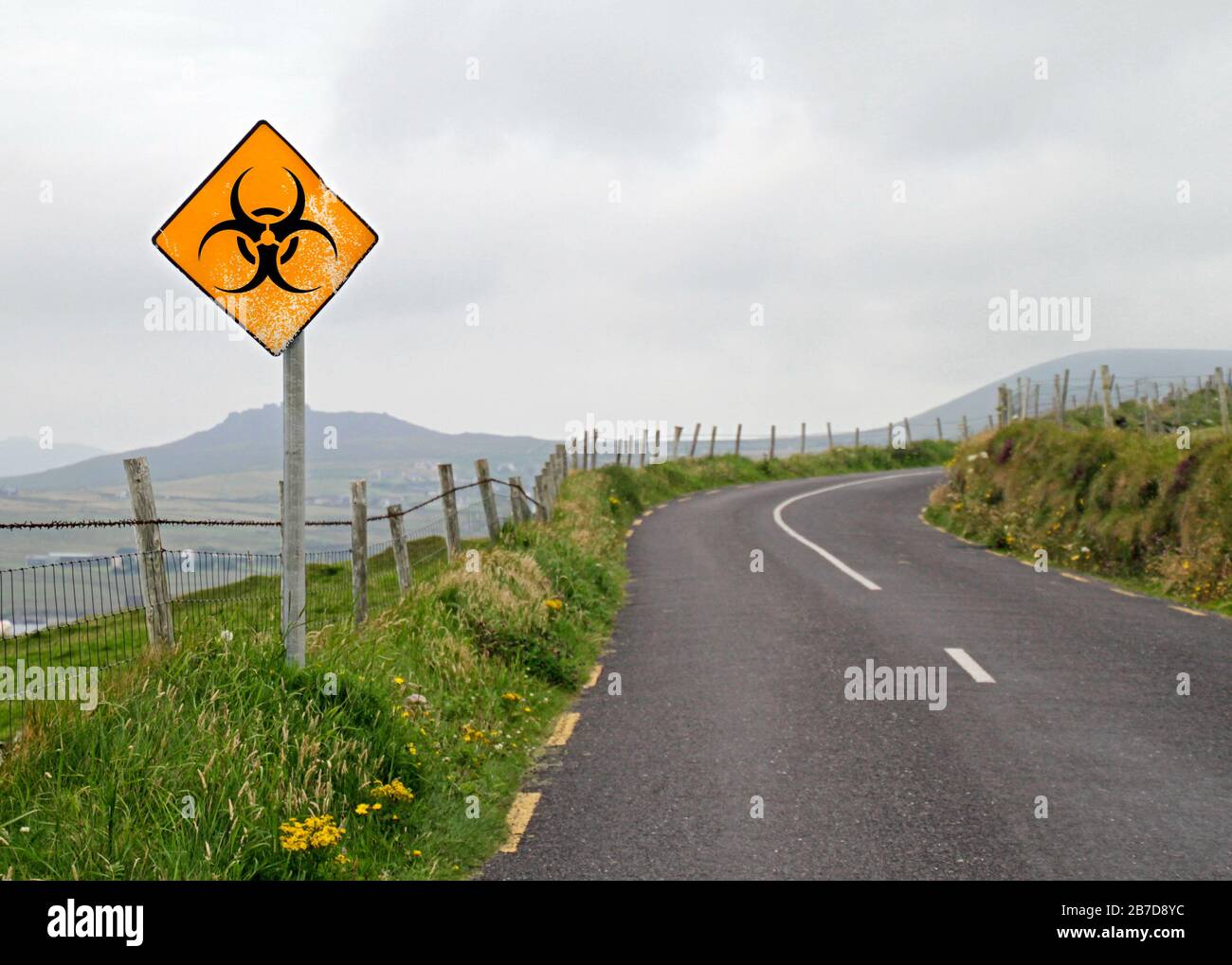 Cartello stradale con simbolo di pericolo biologico davanti a una curva ...