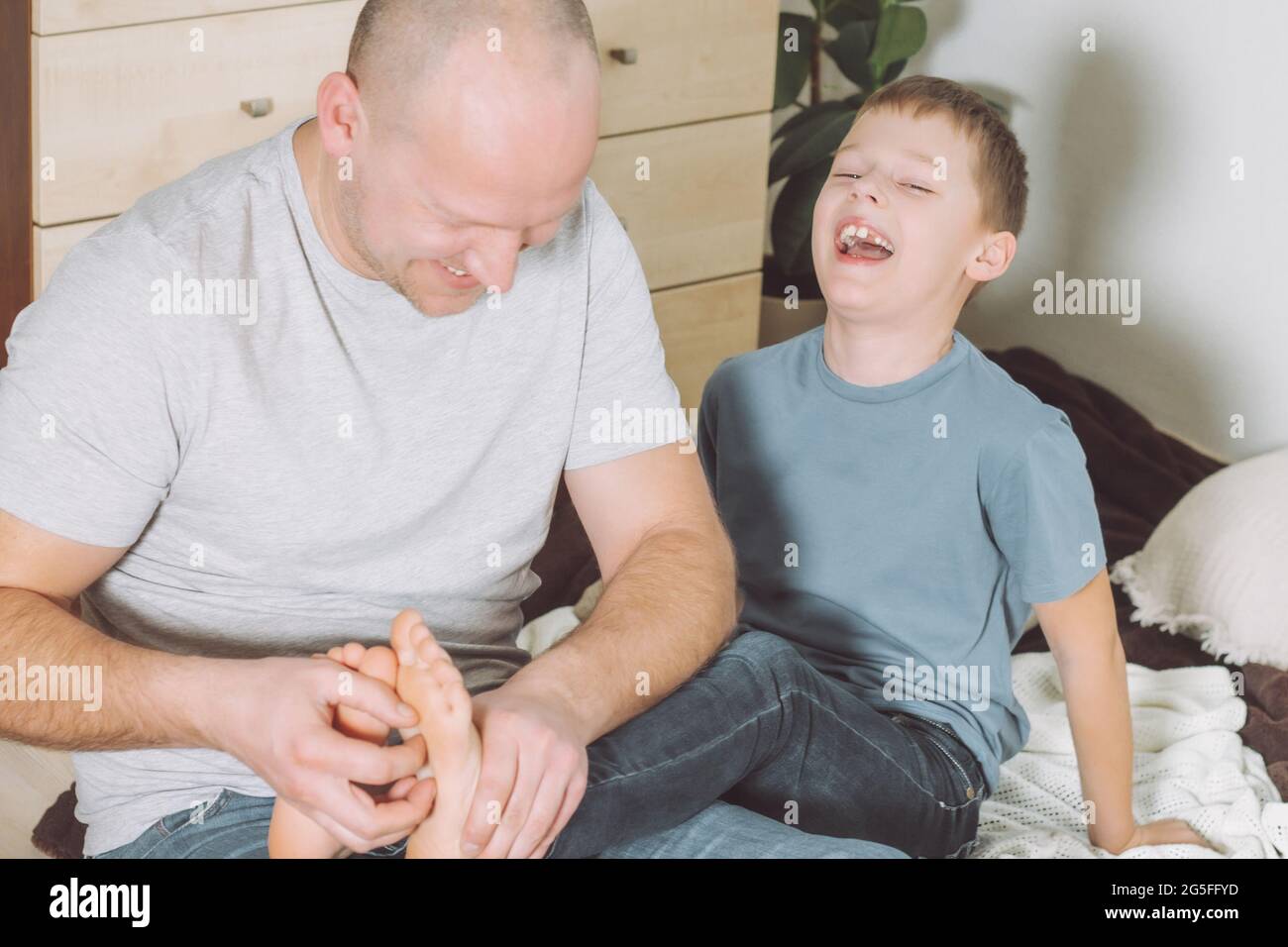 Padre gioca con suo figlio 7-10 seduto sul pavimento. Papà solletico i ...