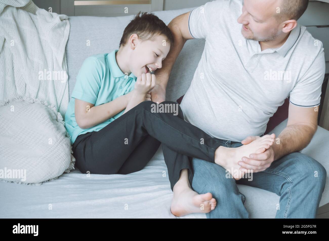 Padre gioca con suo figlio 7-10 seduto sul divano. Papà solletico i ...