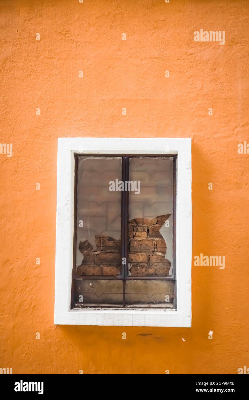 Vetro rotto in finestra su parete in cemento intonaco color arancio con ...