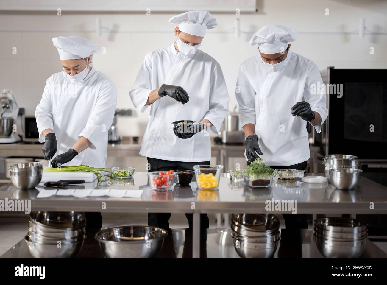 Tre chef ben vestiti in maschere per il viso preparano cibo da asporto ...