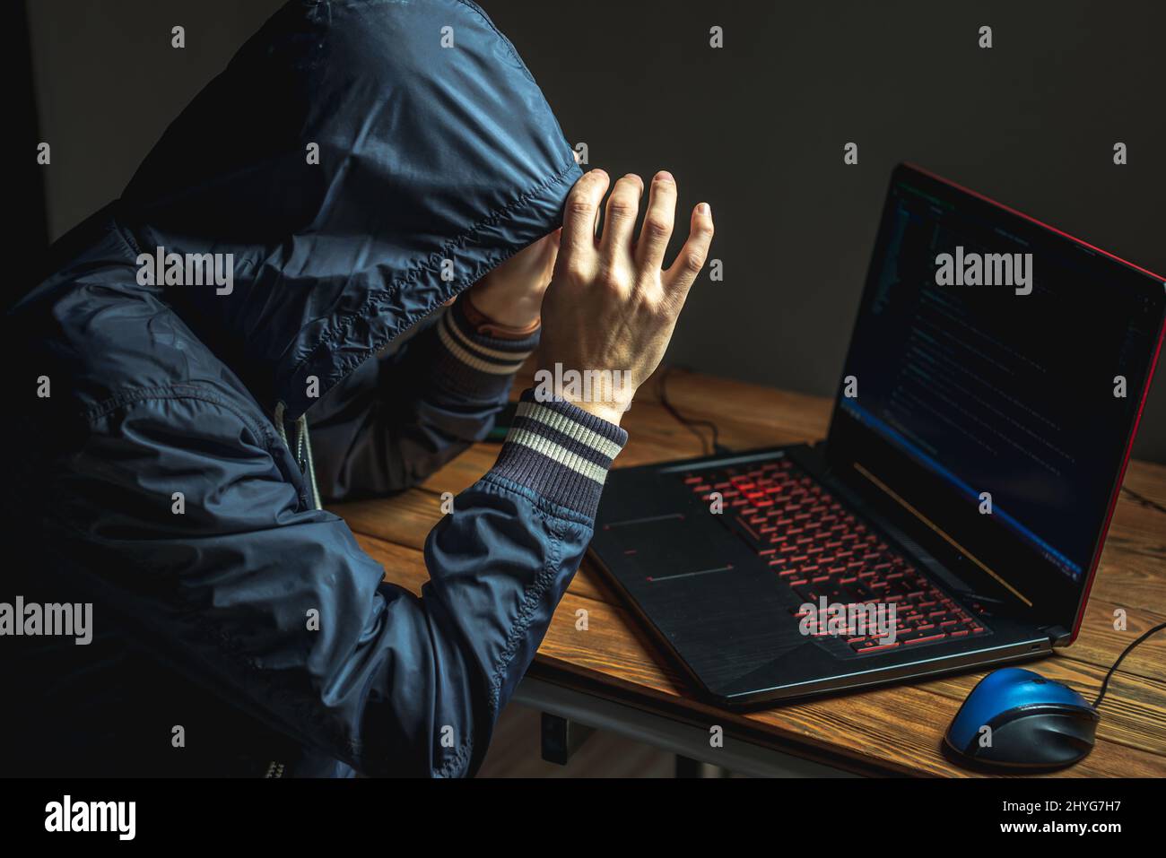Un hacker in un cappuccio con un telefono sta digitando su una tastiera ...
