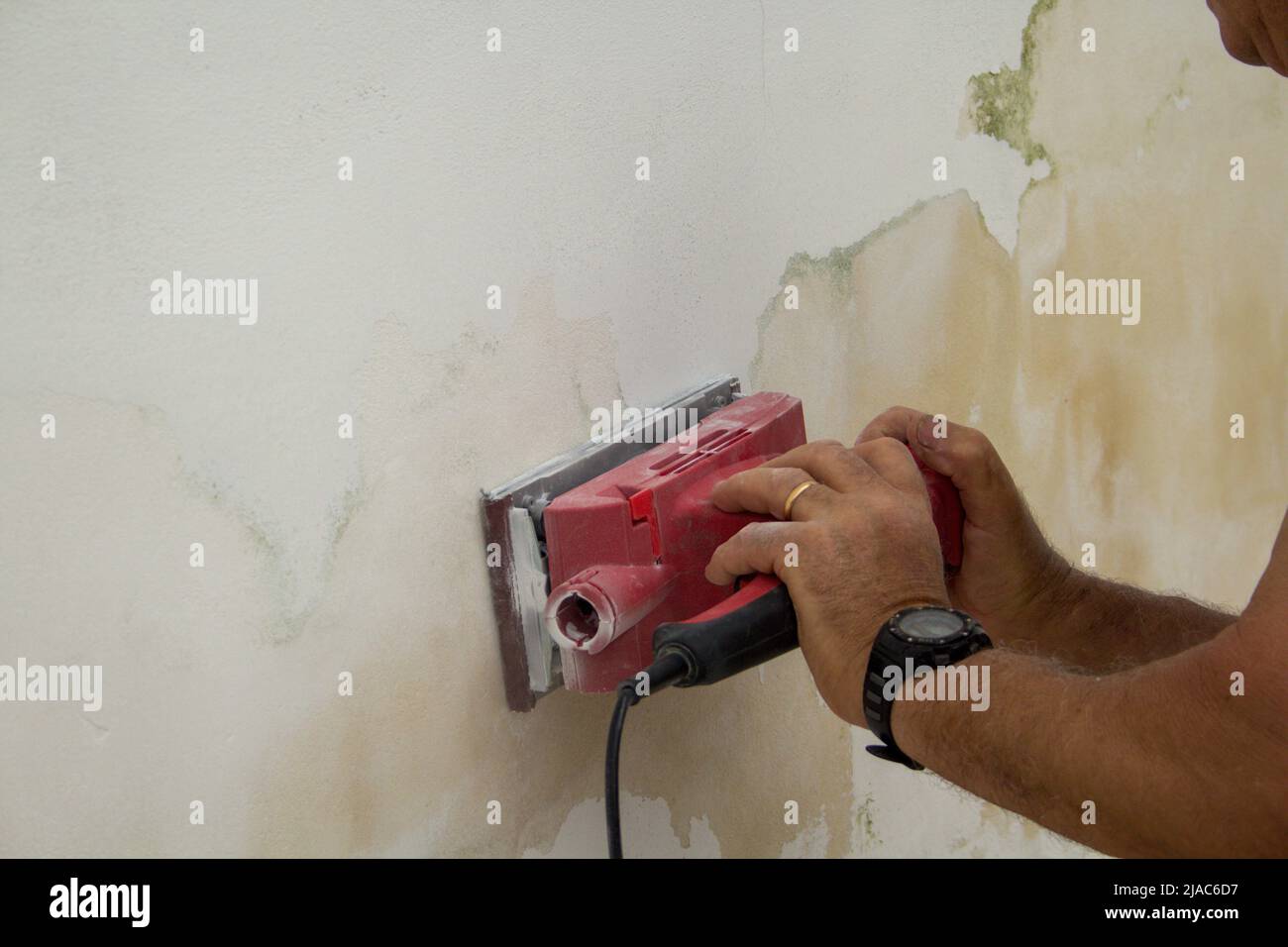Immagine delle mani di un uomo che rimuove intonaco e muffa da un muro ...
