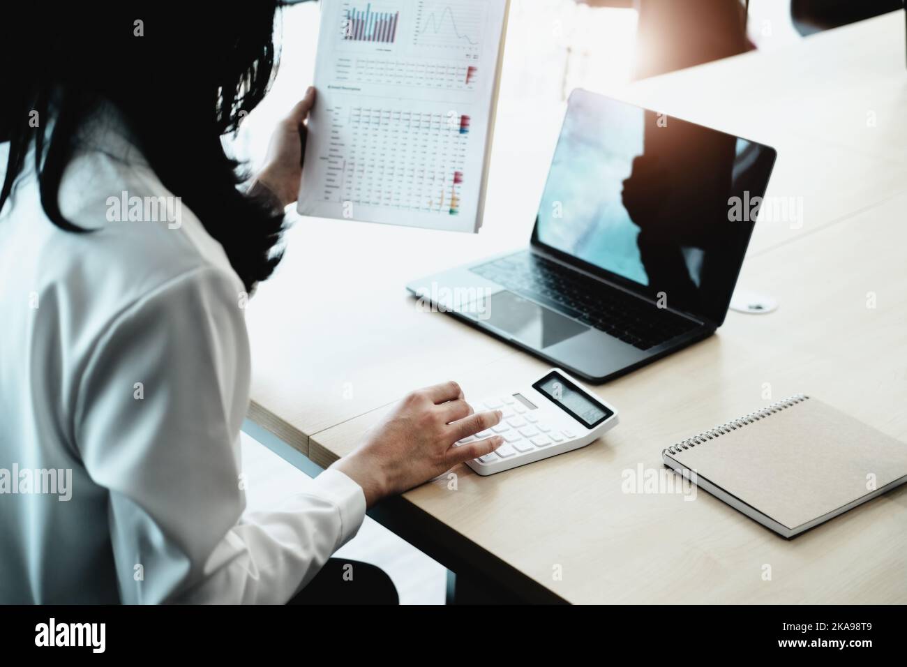 Donna d'affari che usa la calcolatrice per rivedere il bilancio annuale ...