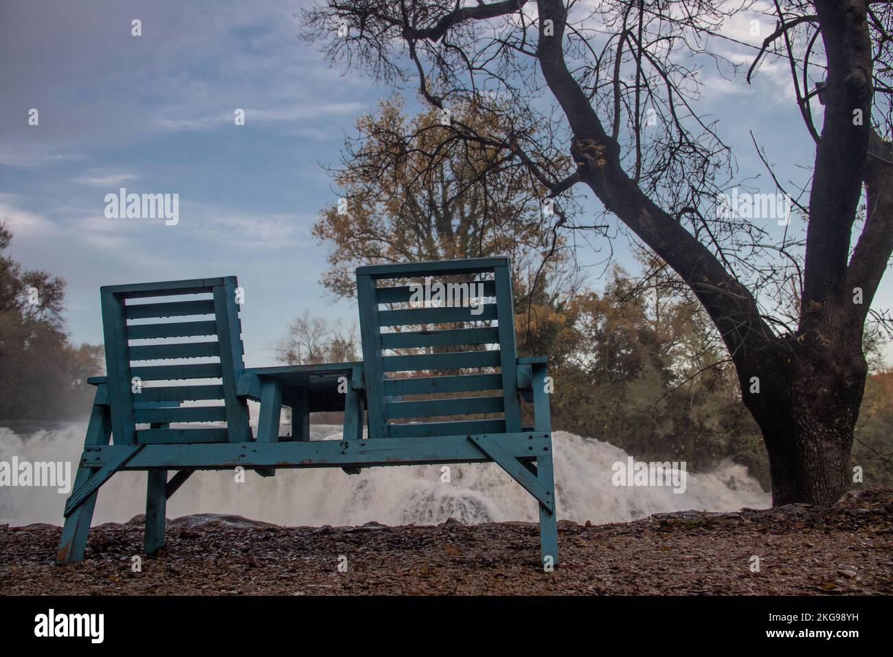 Panca in legno dipinta di blu accanto alla riva della cascata di fiume ...