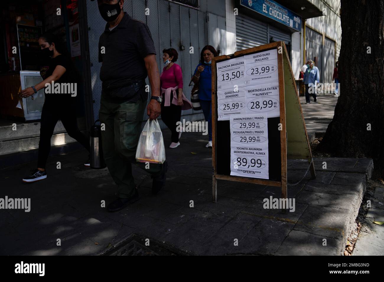Pedestrians walk past a sandwich board sign displaying the prices of ...