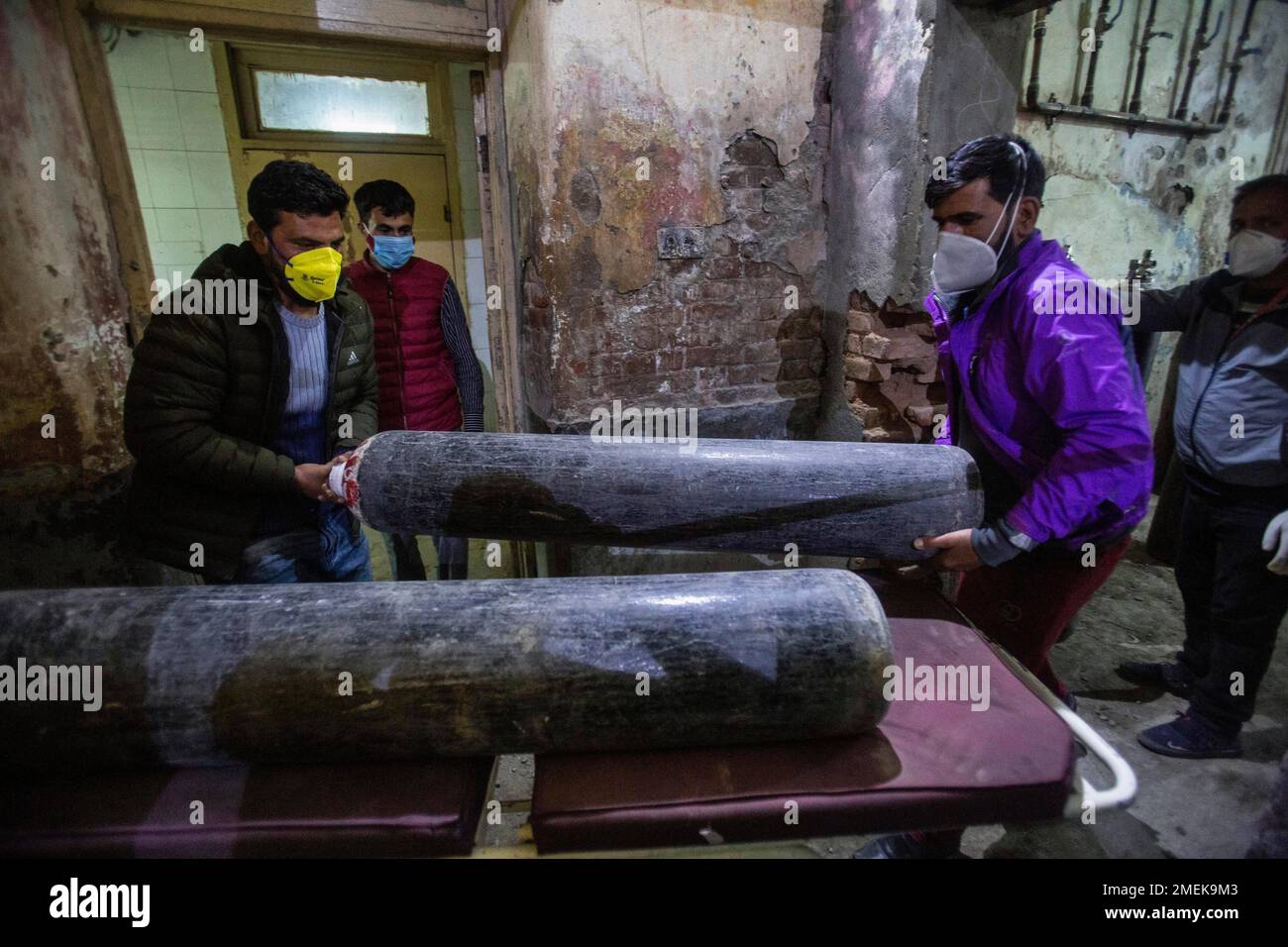 Attendants of a patient carry an oxygen cylinder for the patient inside ...
