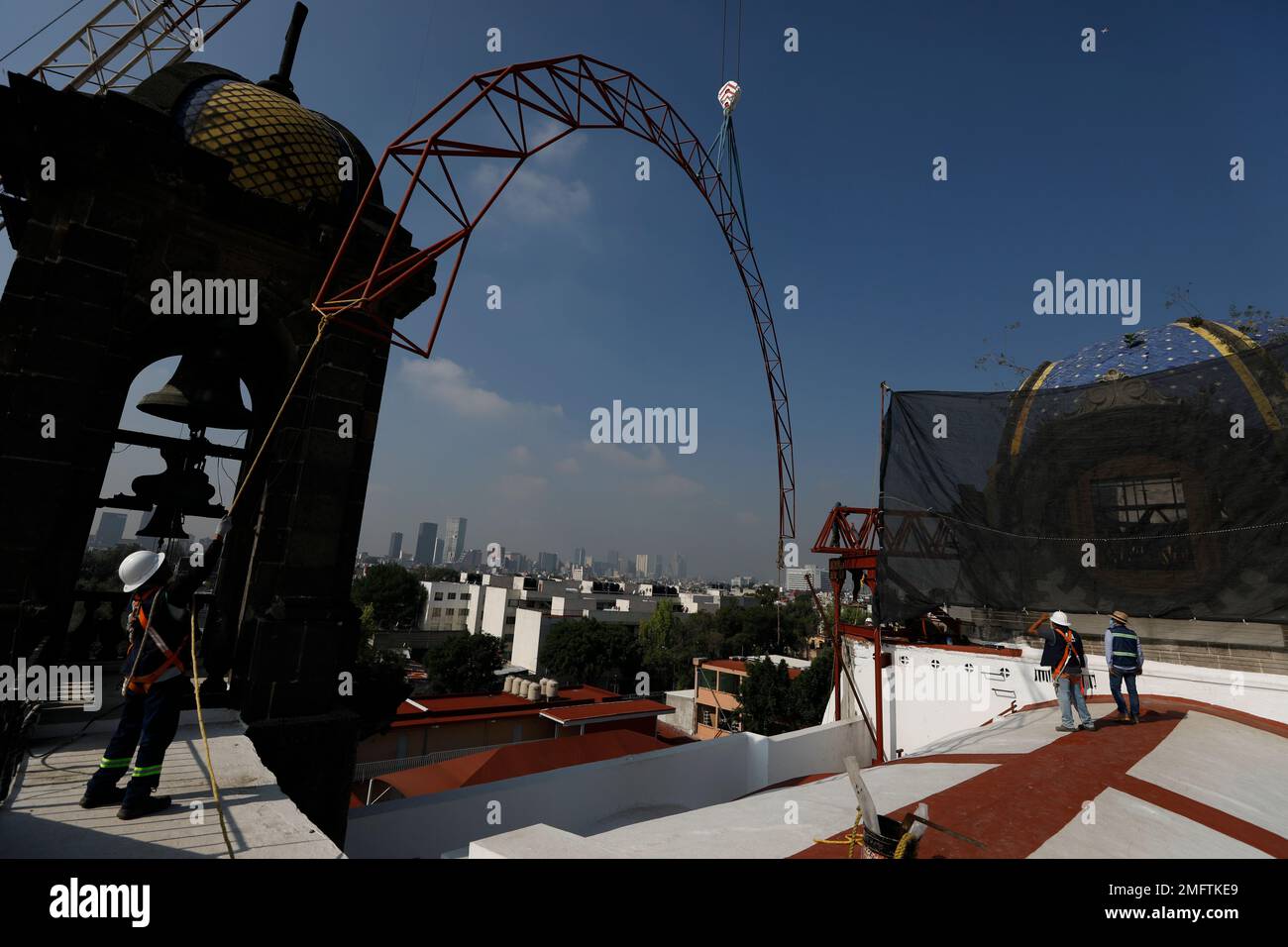 A worker guides a steel arch being lifted by a crane into place overtop ...