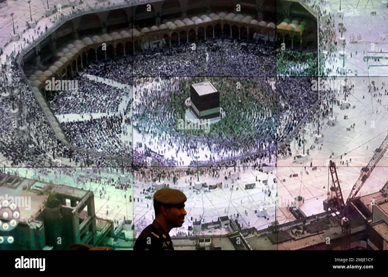 A Saudi police officer walks past a giant screen displaying the Kaaba ...