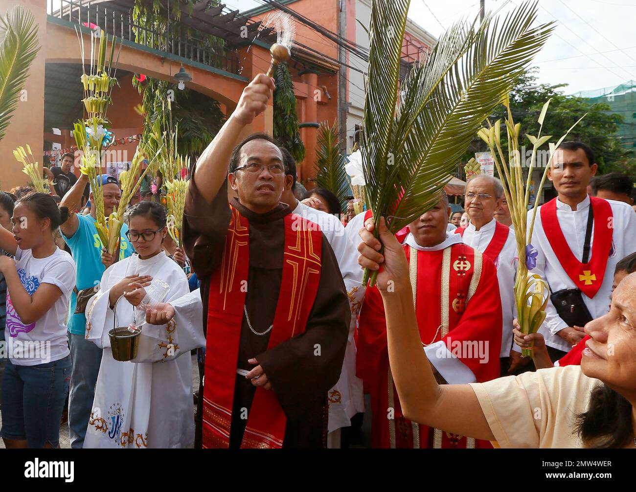A Roman Catholic priest blesses with holy water devotees waving palm ...