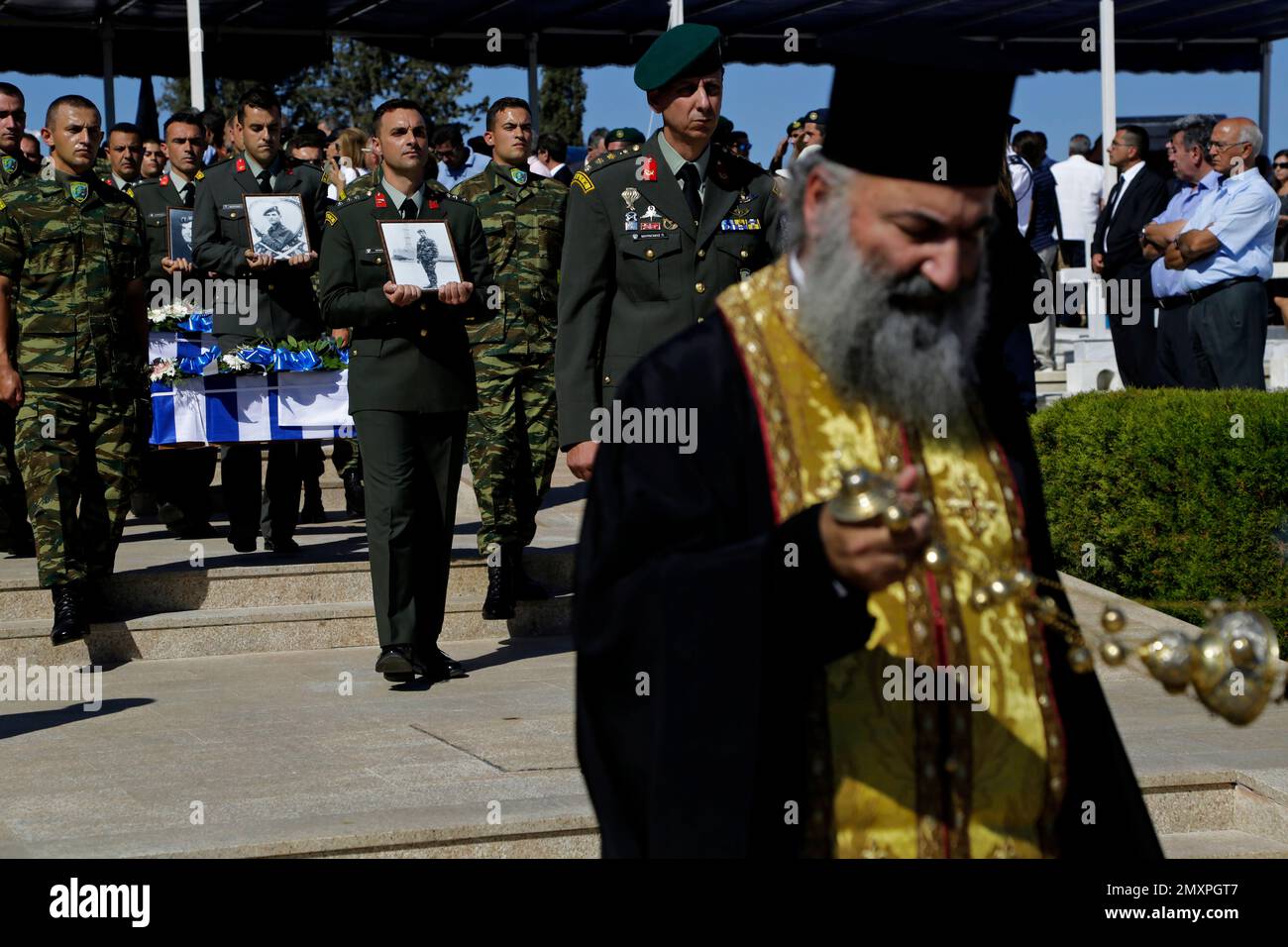 A Greek Orthodox priest, right, walks with Greek soldiers carrying the ...