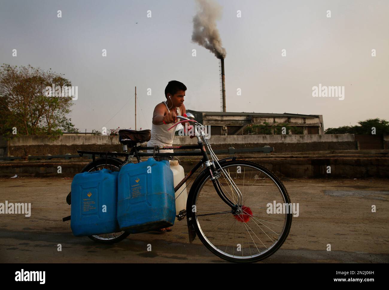 An Indian man pushes a cycle carrying water cans as smokes rises from a ...