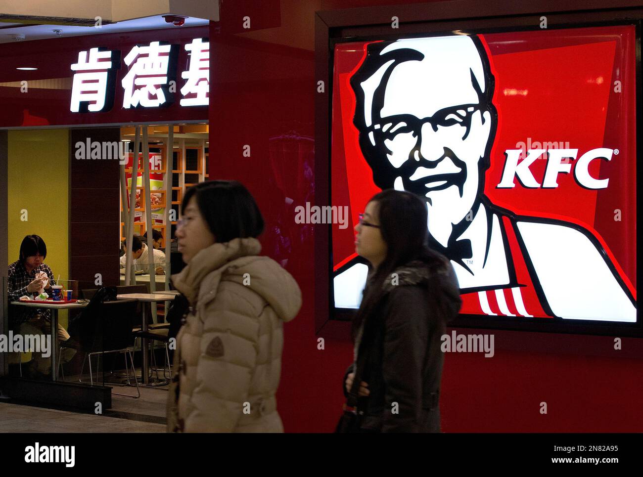 Chinese women walk past a customer eating inside a KFC restaurant at a ...