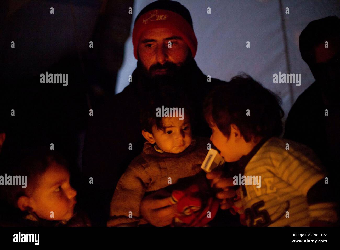 A Syrian man holds his children as they warm themselves at a refugee ...