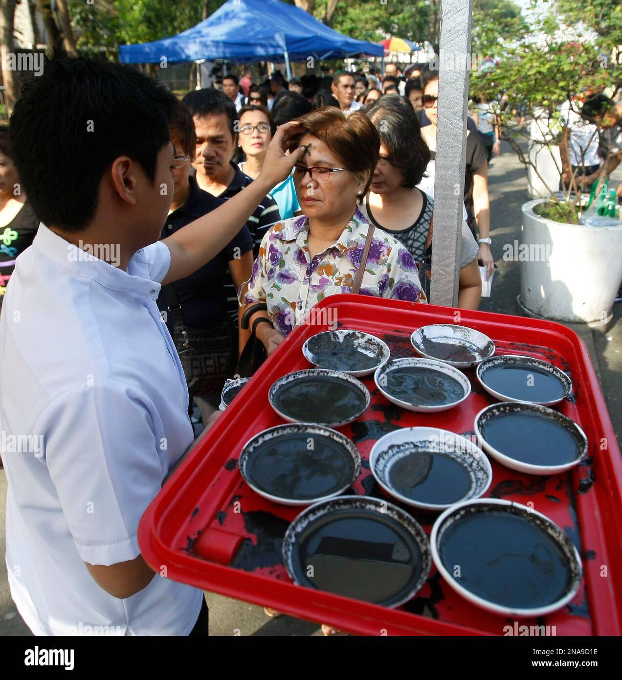 A Catholic lay leader marks the foreheads of devotees with black ashes ...