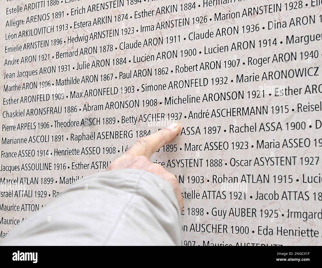 A visitor points to the name of a relative on one of the pale stone ...