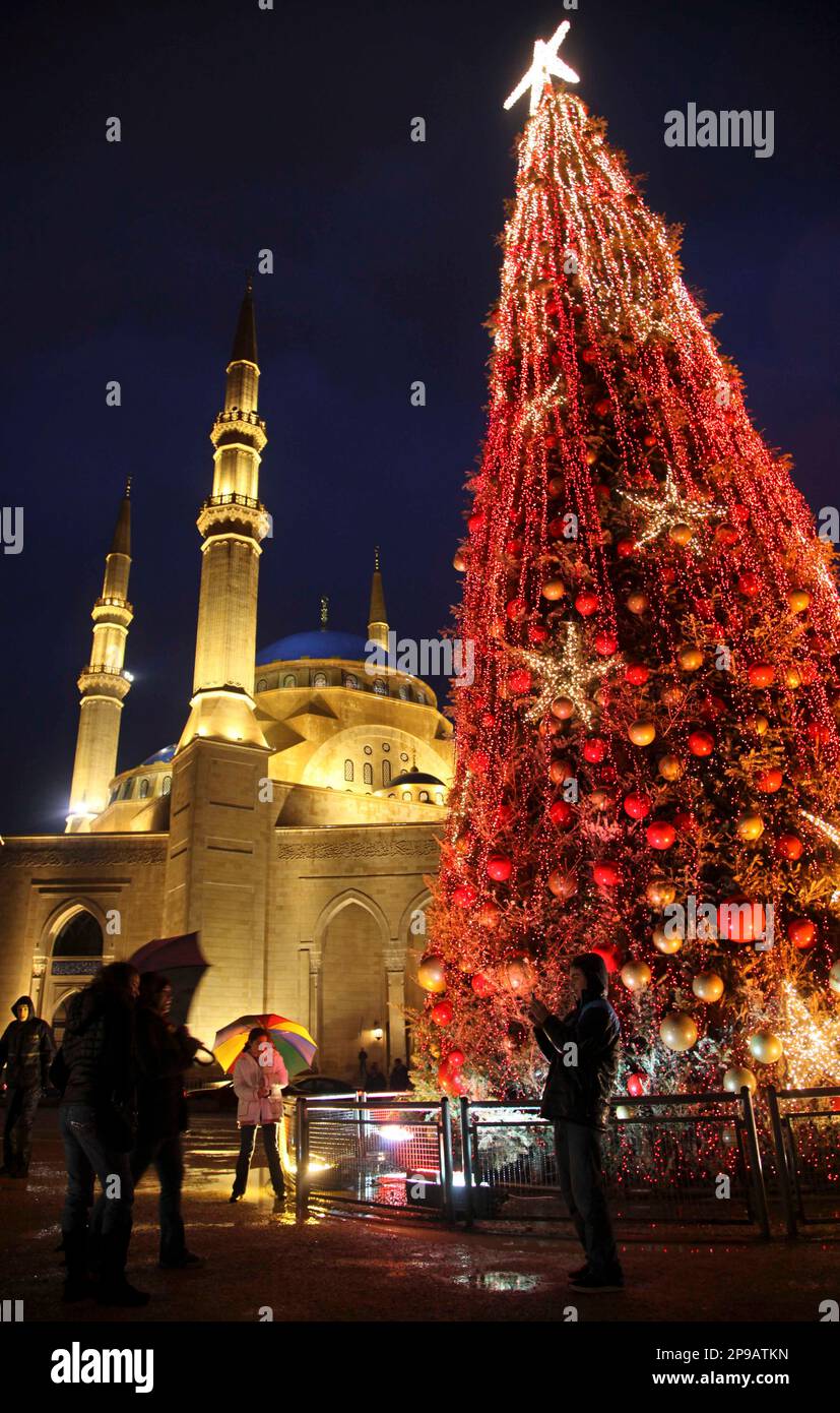 Passers-by pose for photographs by a huge Christmas tree next to ...