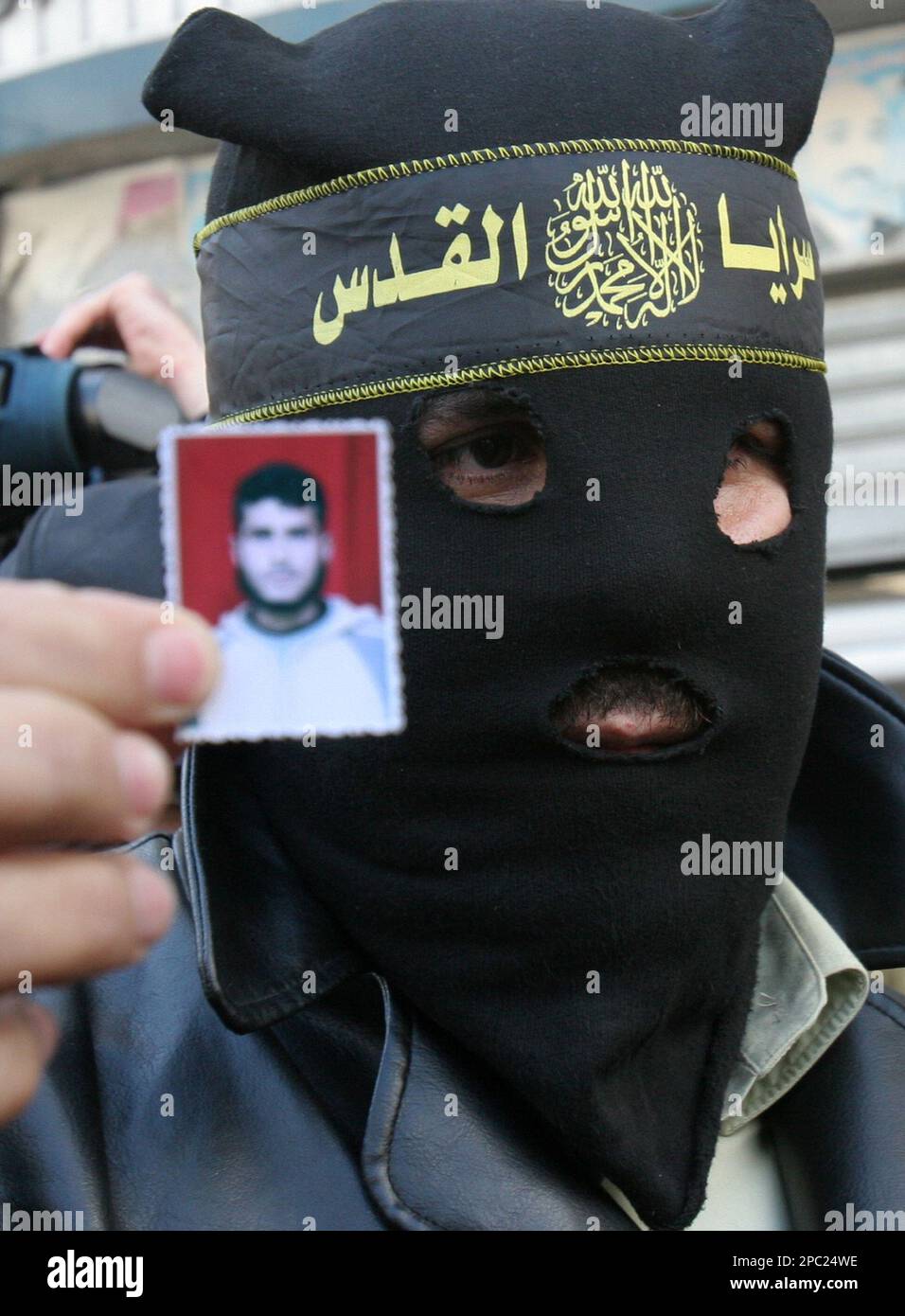 A Palestinian masked militant of Islamic Jihad holds a photo of ...
