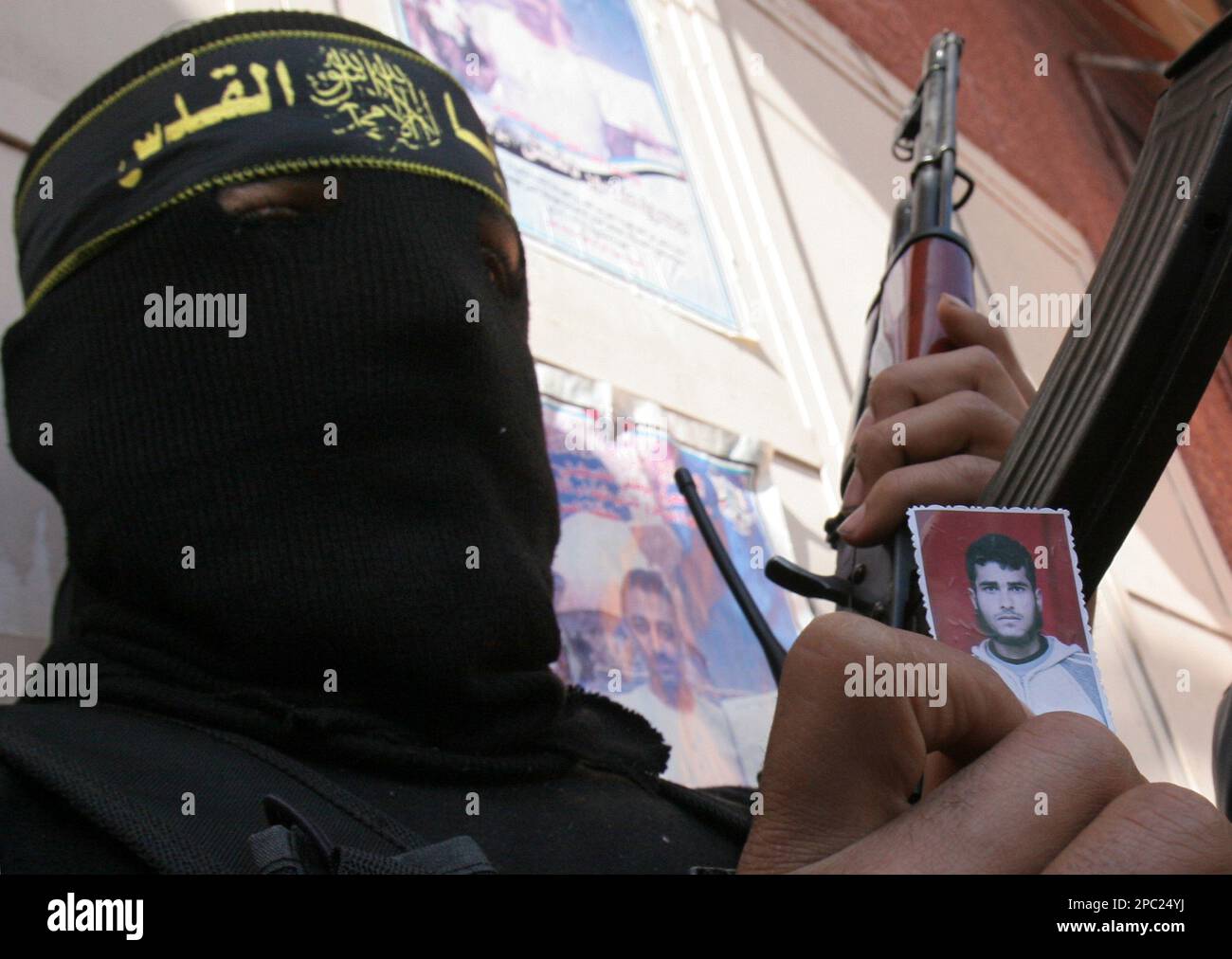 A Palestinian masked militant of Islamic Jihad holds a photo of ...