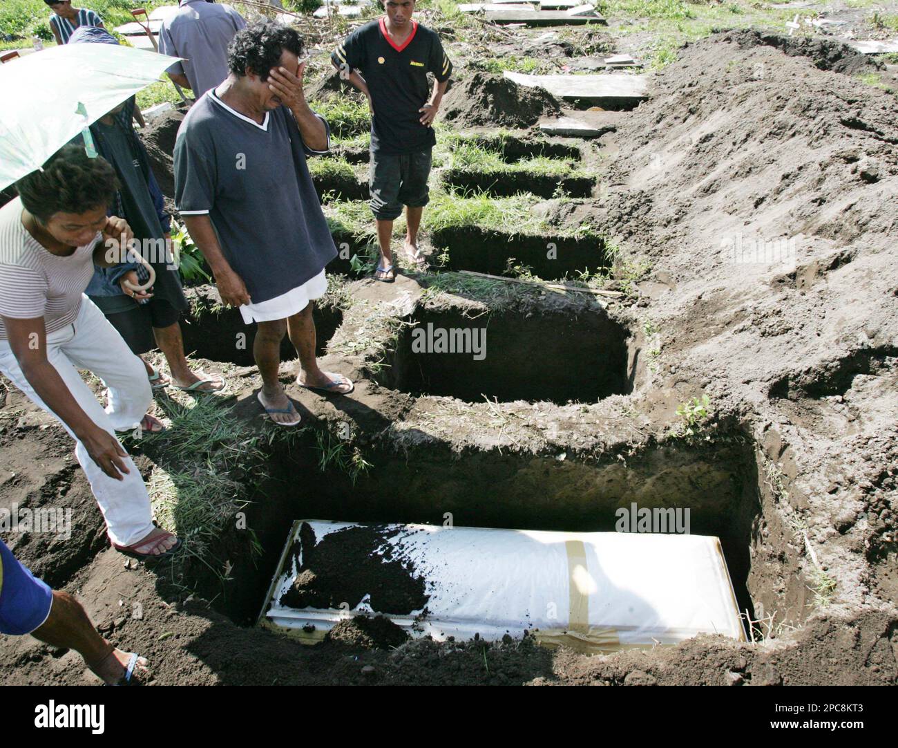 Carlito Valderama, second from right, cries as earth is shoveled on the ...