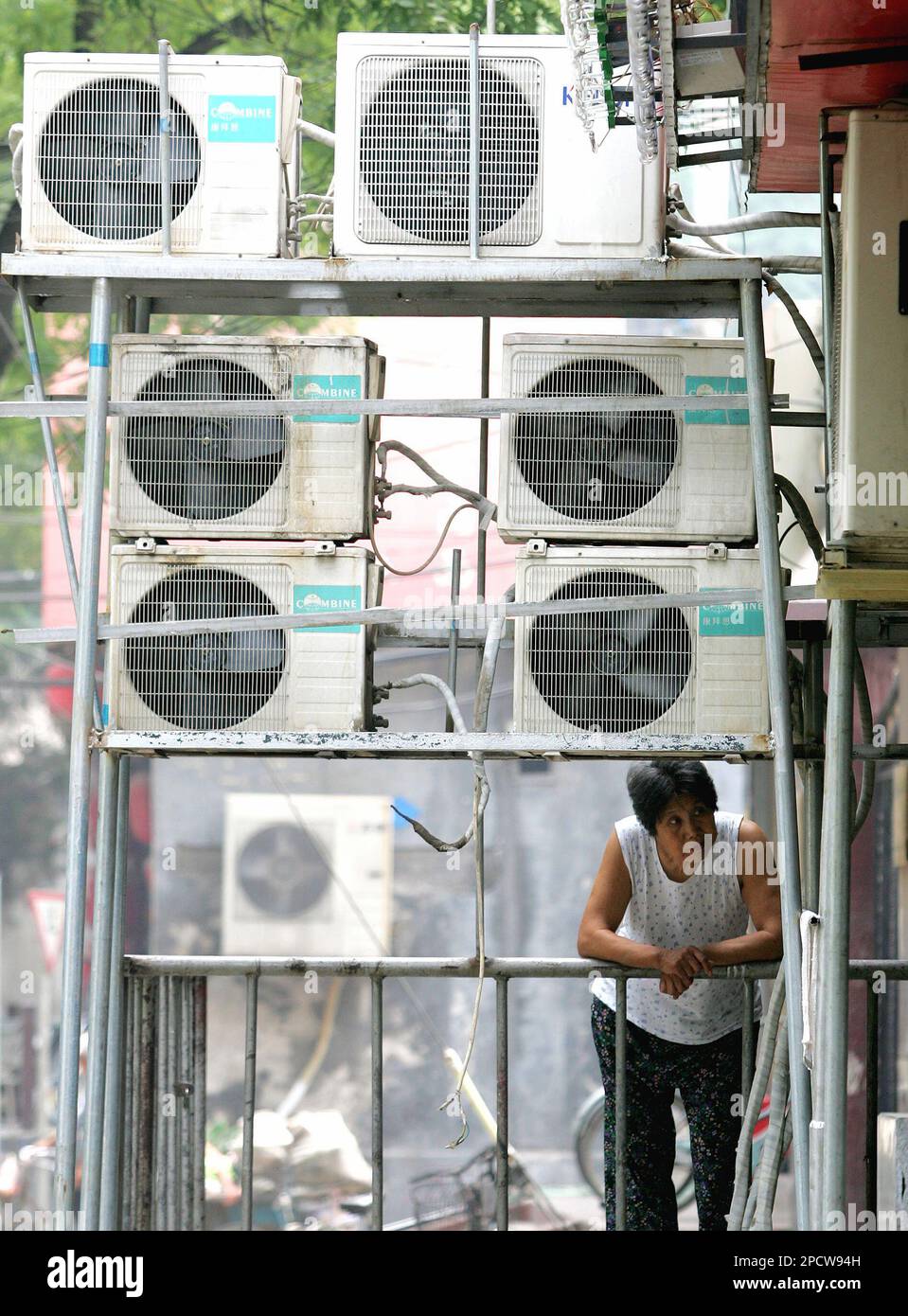 A woman rests below a stack of air conditioning units outside a ...