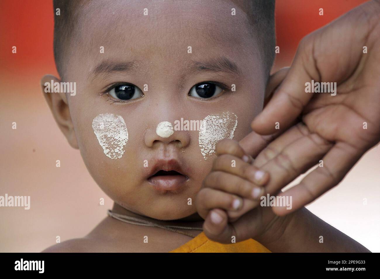 A young girl, her face painted with traditional makeup, looks on as she ...